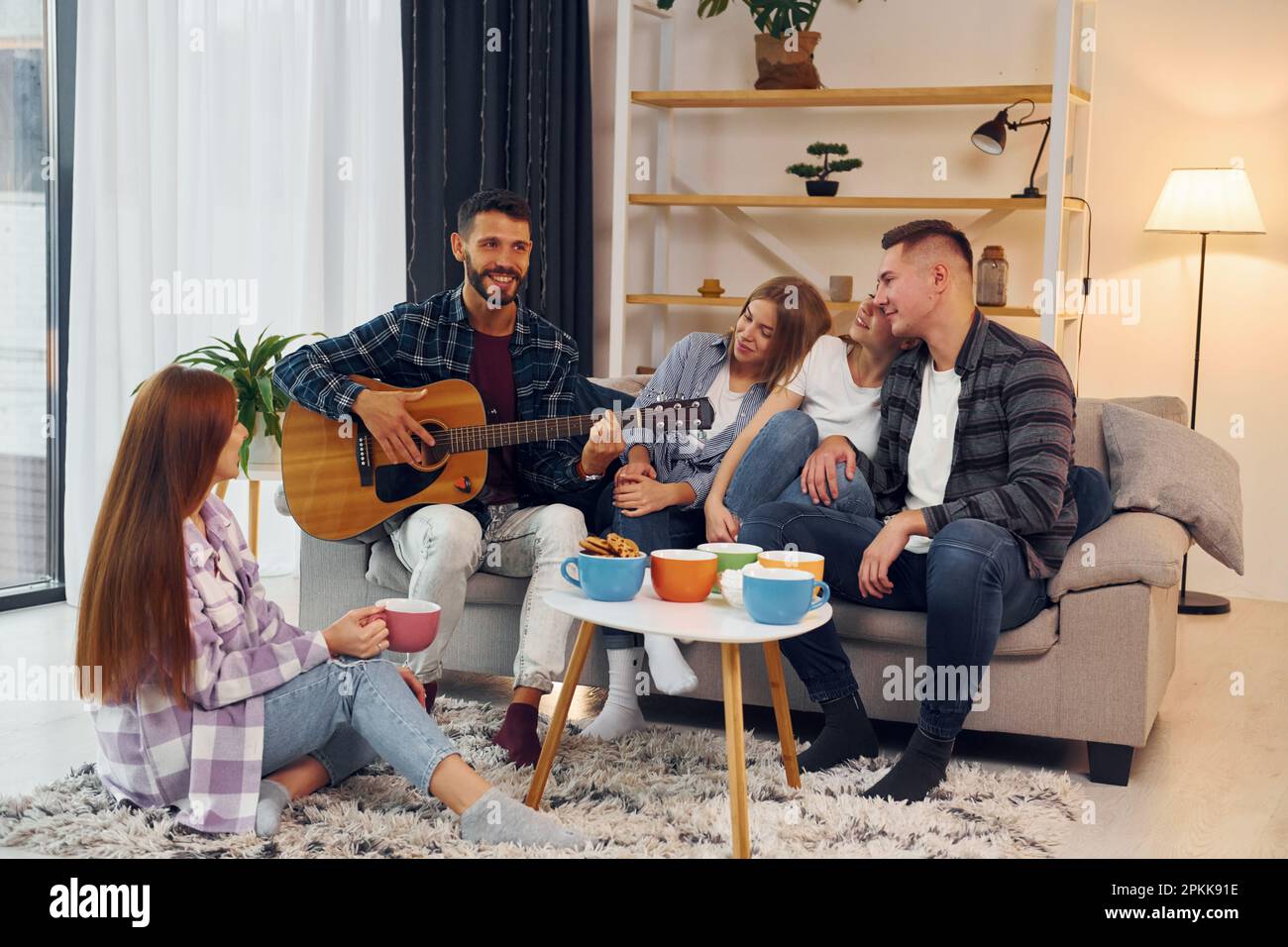 Playing acoustic guitar. Group of friends have party indoors together ...