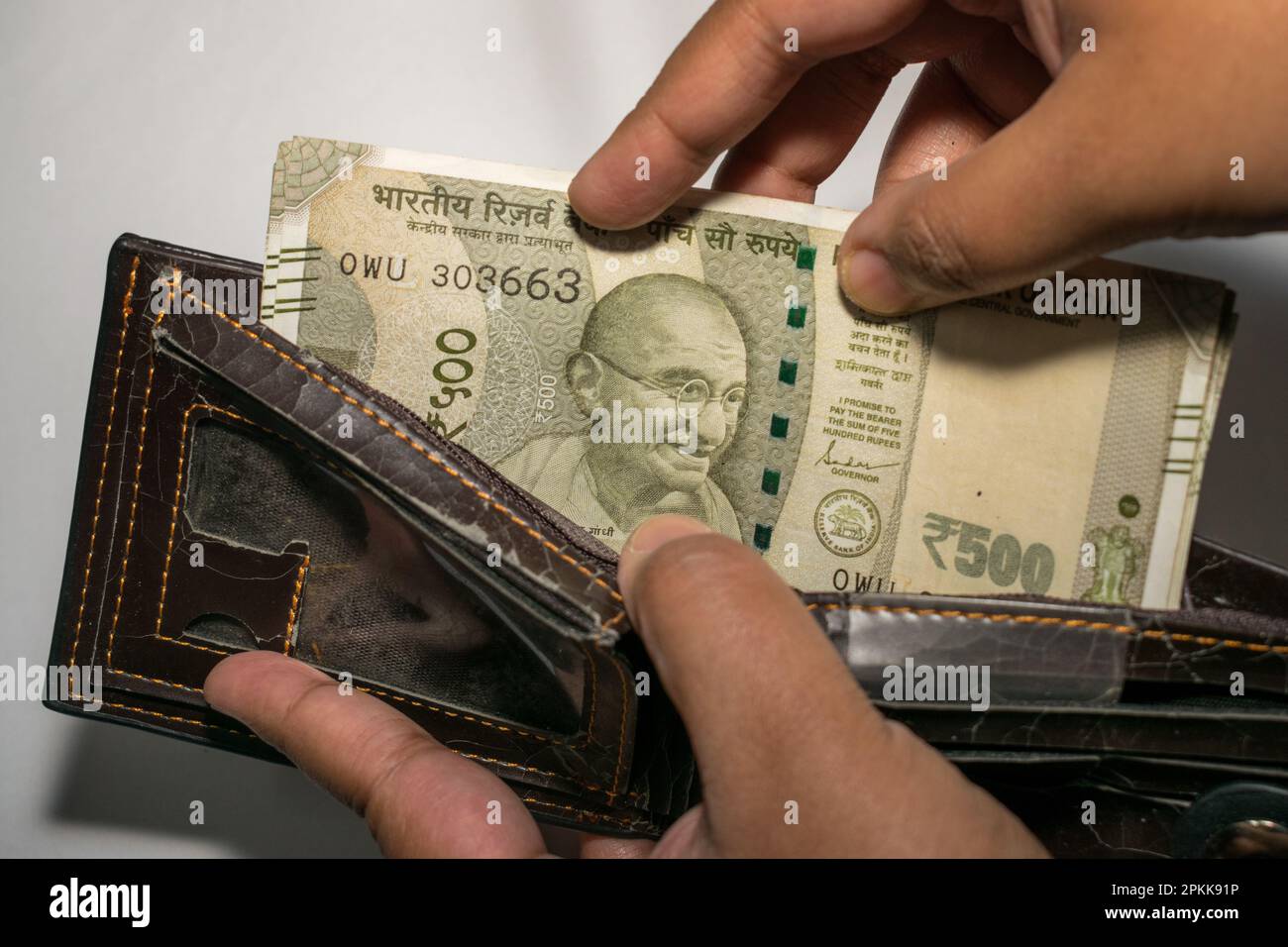A hand inserting five hundred rupee Indian banknotes in a wallet on a ...