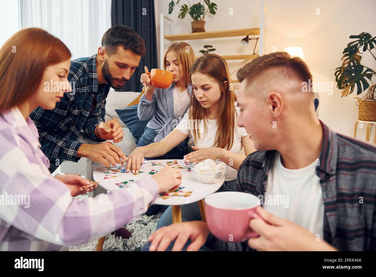 Focused at puzzle game. Group of friends have party indoors together ...