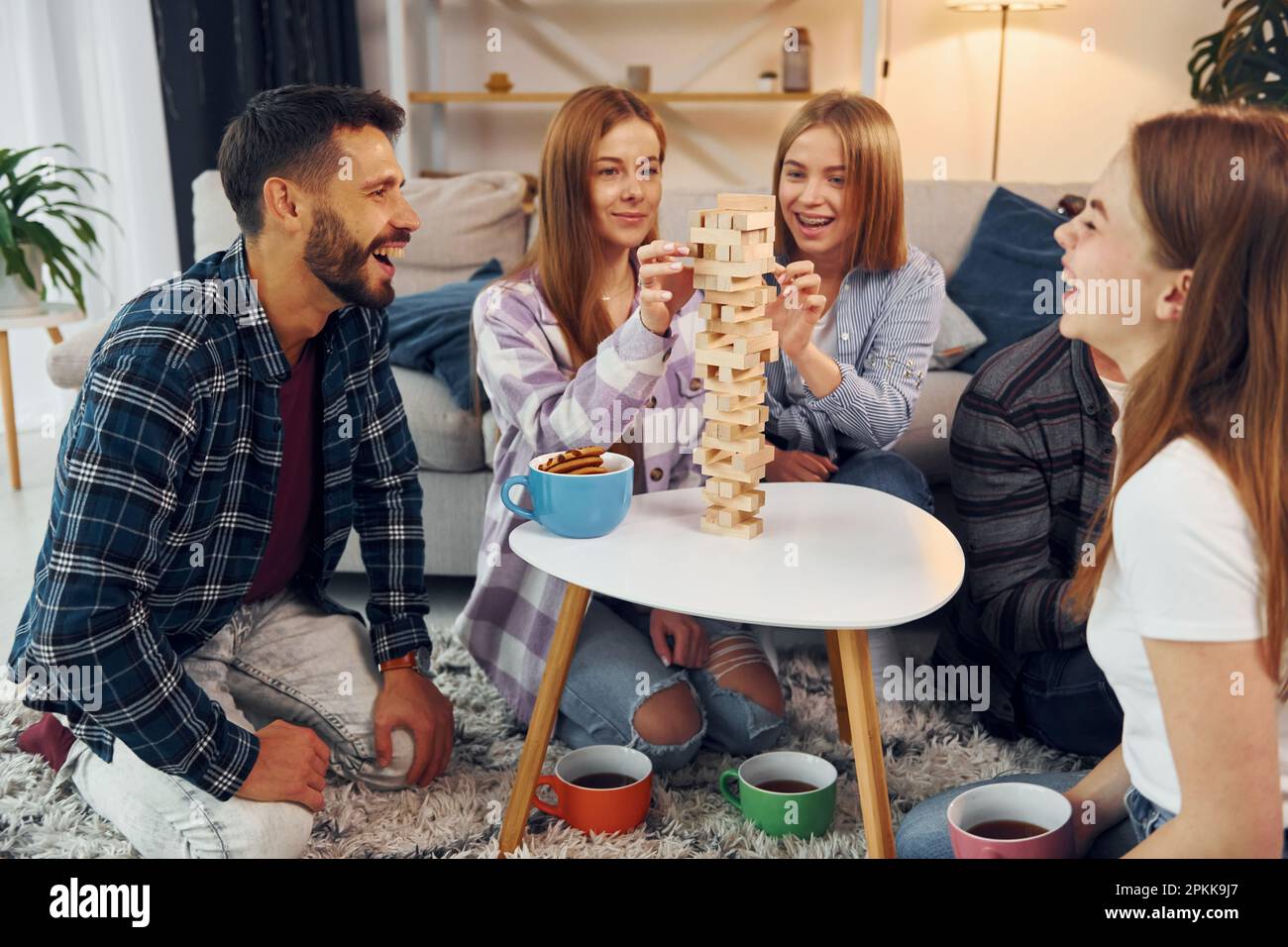 Wooden tower game on the table. Group of friends have party indoors ...