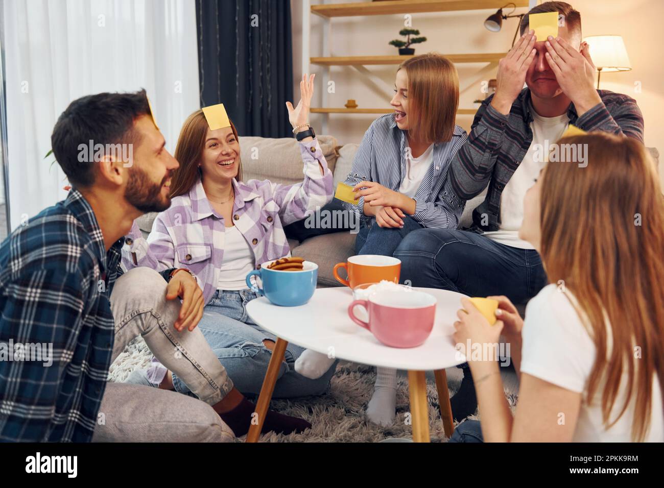 Yellow stickers on forehead. Group of friends have party indoors ...