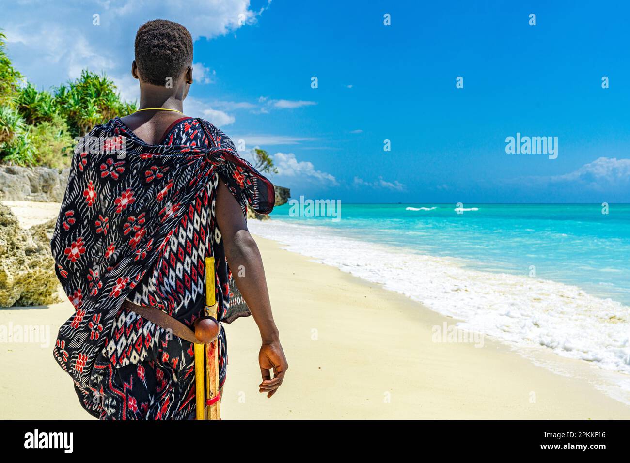 Maasai man with traditional clothing and stick admiring the crystal sea ...
