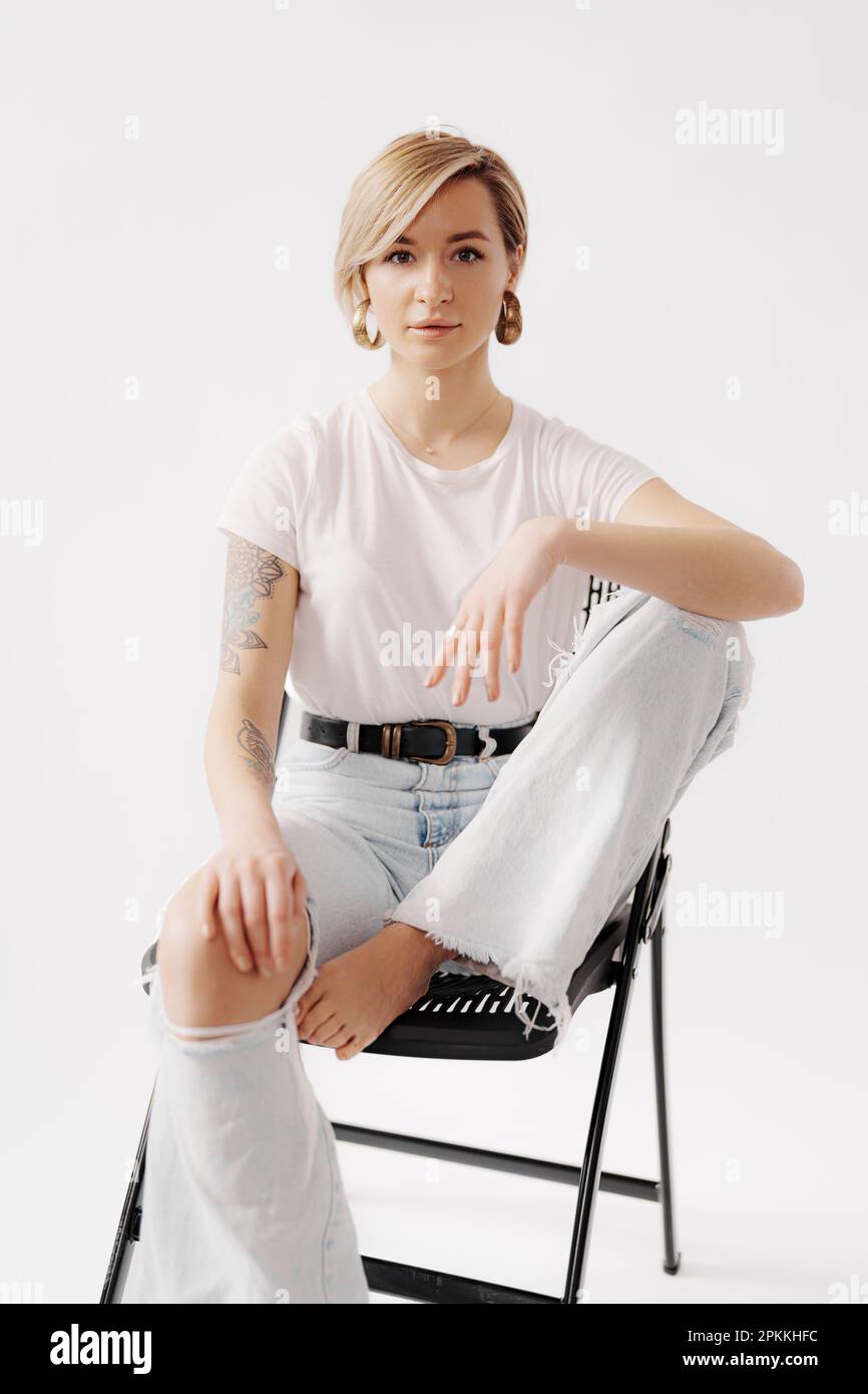 Stylish woman sitting on chair with hands on knees Stock Photo - Alamy