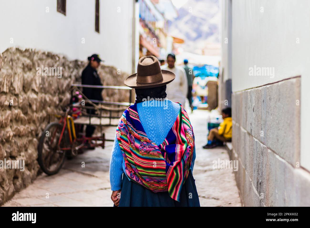 Woman walking away in narrow street with traditional colorful Peruvian ...