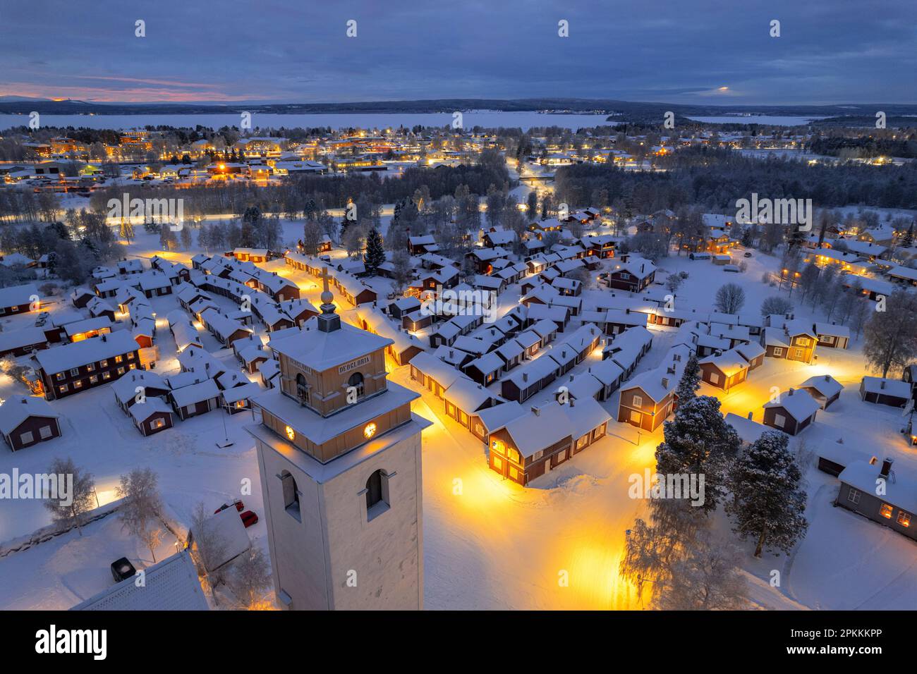 Aerial view of illuminated cottages and bell tower covered with snow in ...