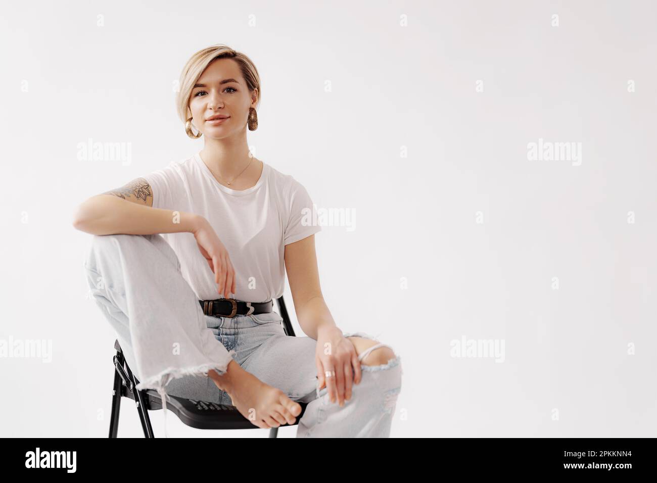 Stylish woman sitting on chair with hands on knees Stock Photo - Alamy