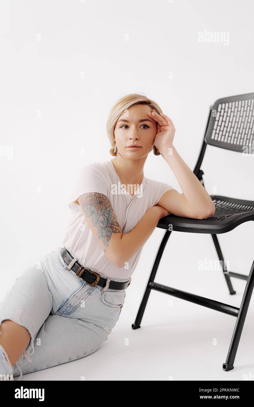 Young woman sitting on floor leaning on chair Stock Photo - Alamy