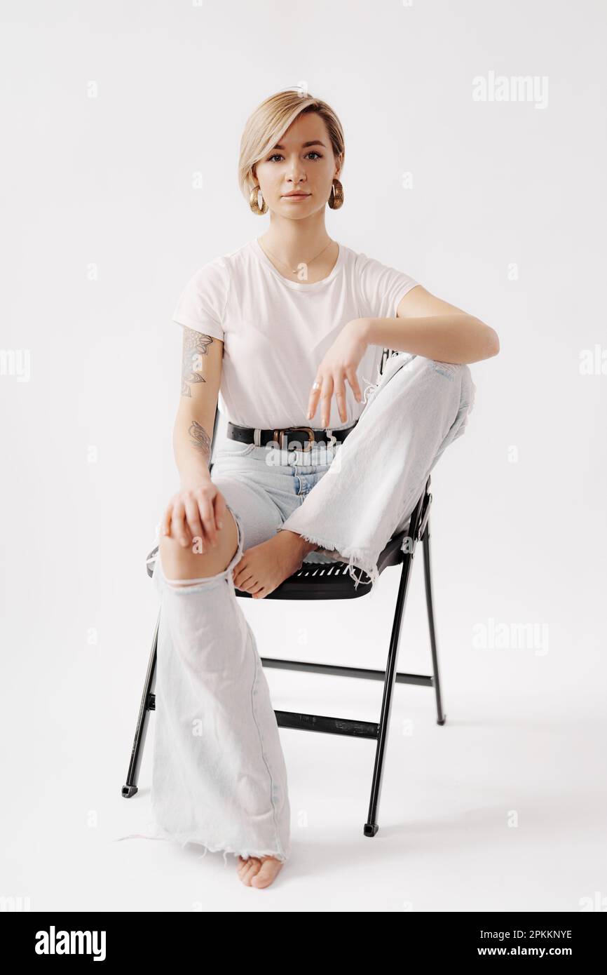 Stylish woman sitting on chair with hands on knees Stock Photo - Alamy
