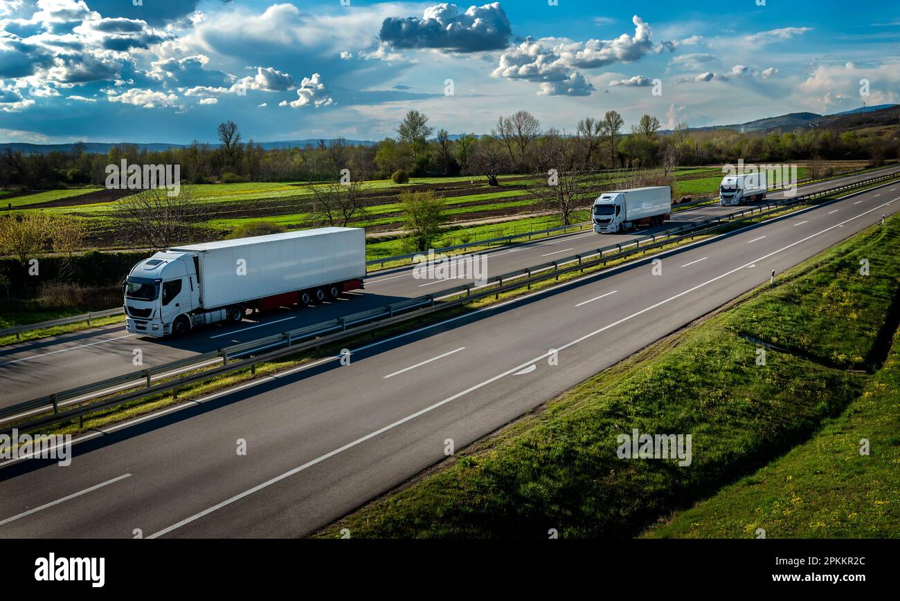 Highway transportation scene with three white transportation trucks in ...