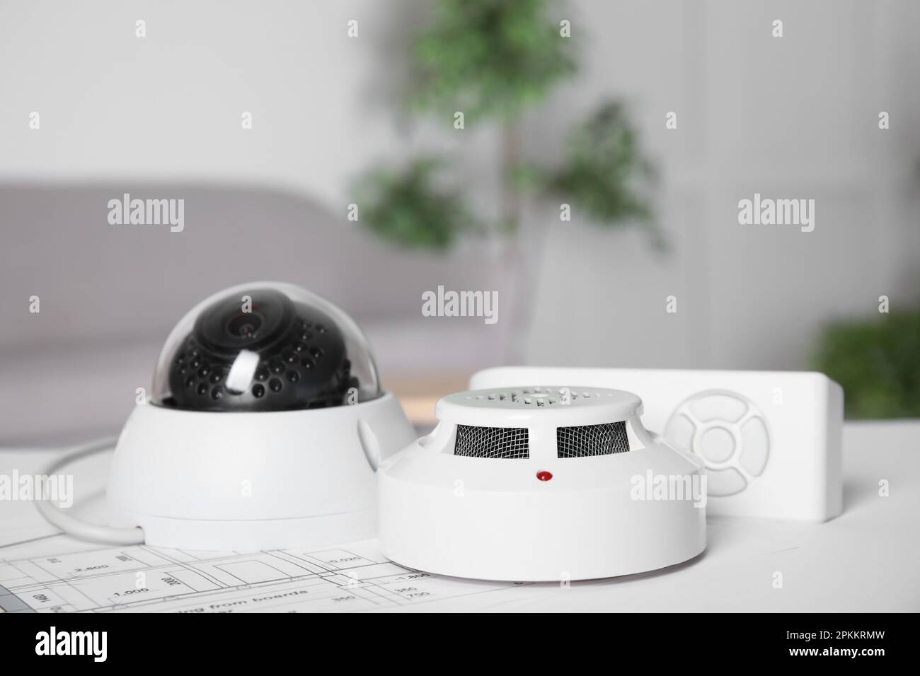 CCTV camera, remote control, smoke detector and building plan on table ...