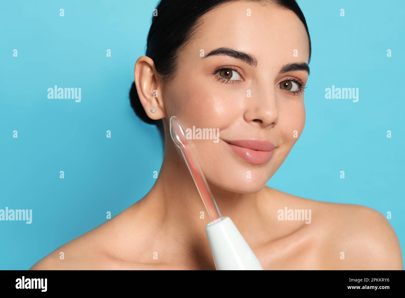 Woman using high frequency darsonval device on light blue background ...
