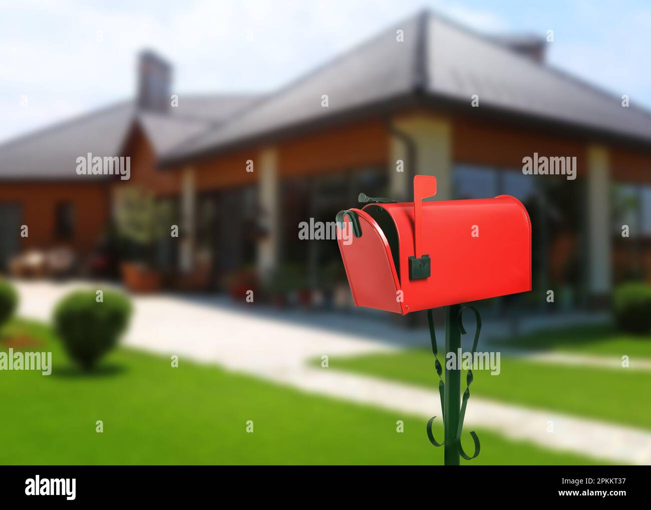 Red letter box and blurred view of modern house with beautiful garden ...