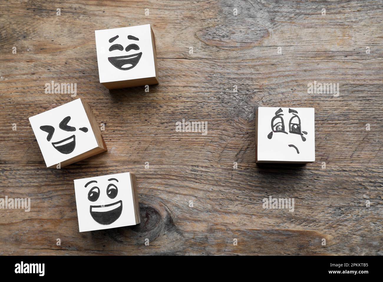 Cubes with sad and funny faces on wooden table, flat lay. Bullying ...