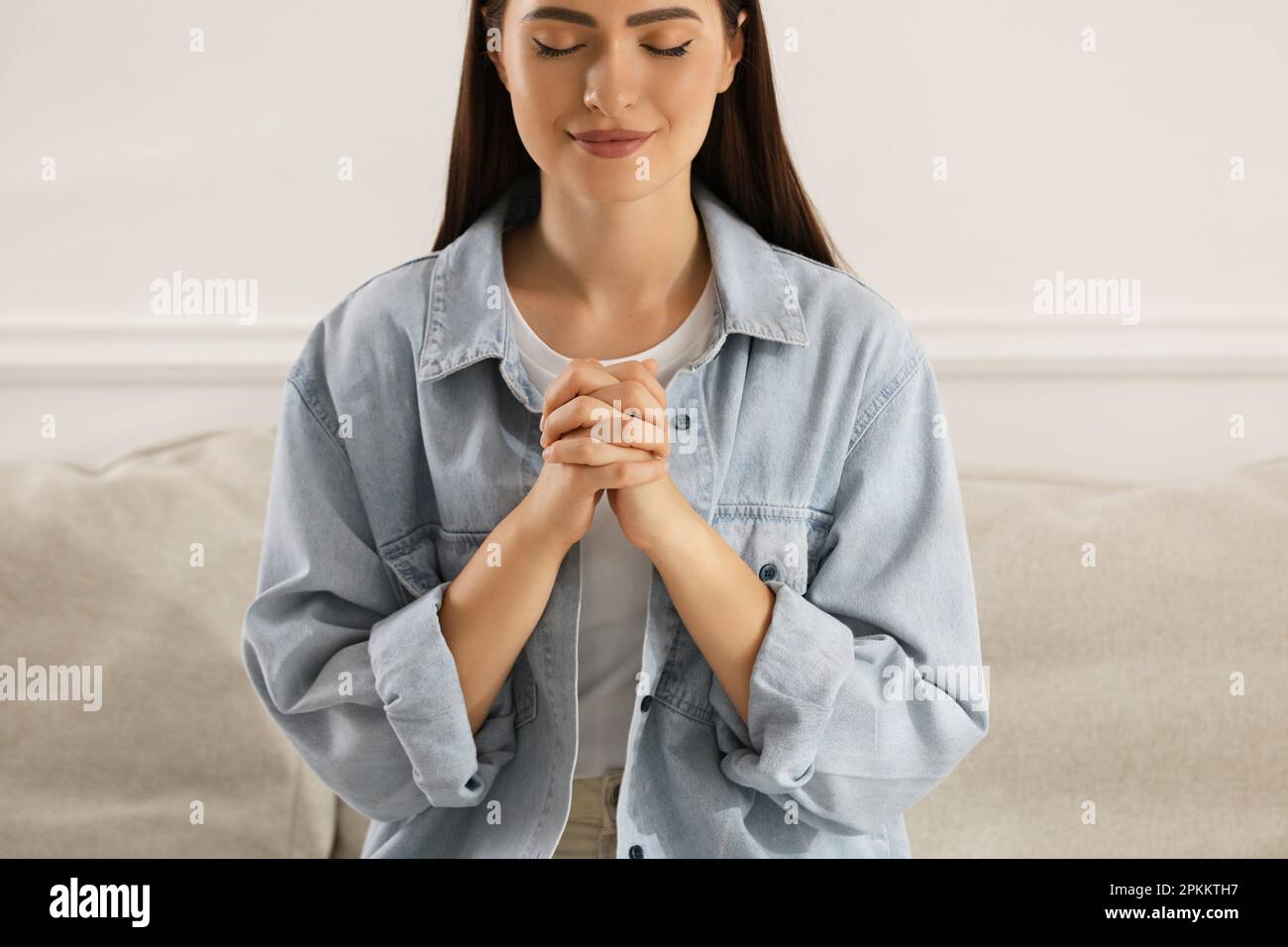 Religious young woman with clasped hands praying indoors, closeup Stock ...