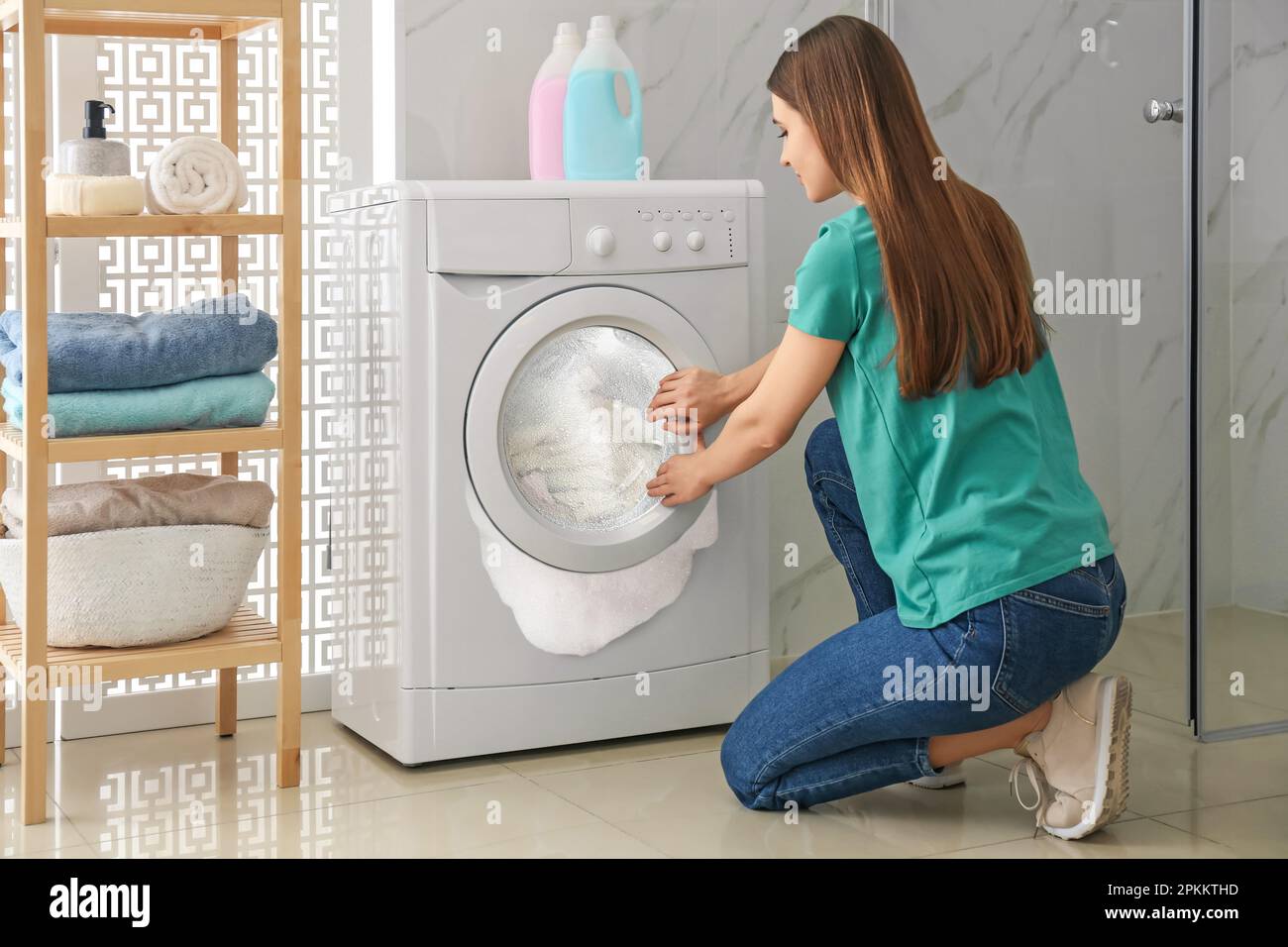 Woman near broken washing machine in room. Foam coming out from drum ...