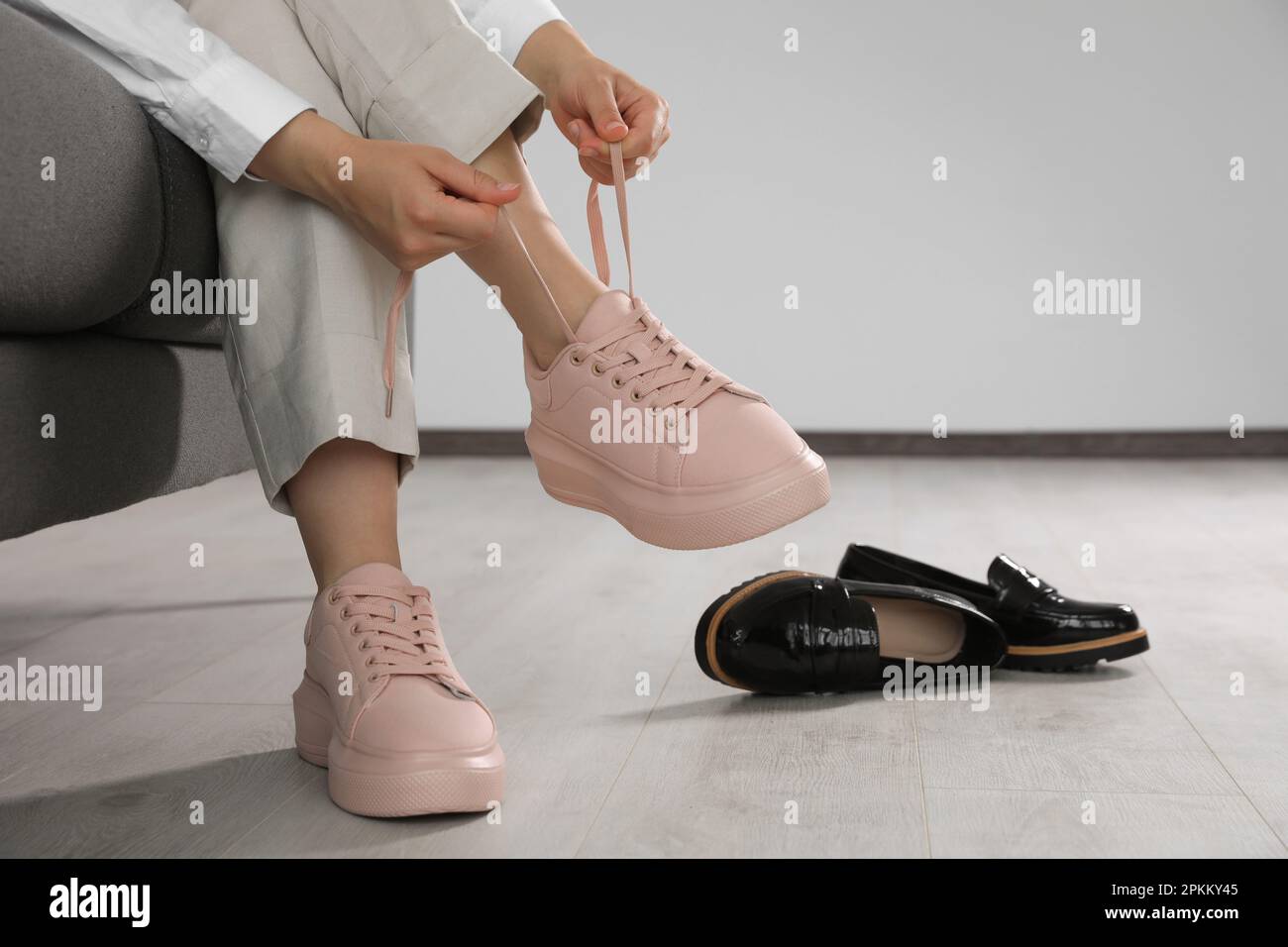 Woman taking off uncomfortable shoes and putting on sneakers in office ...