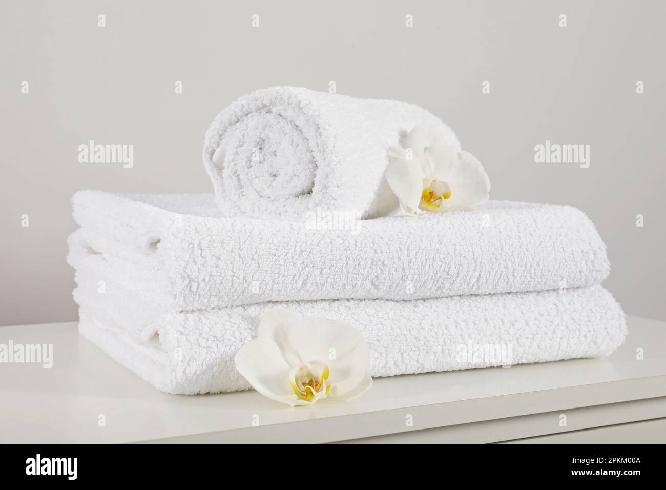 Clean soft white towels with flowers on table against light grey ...