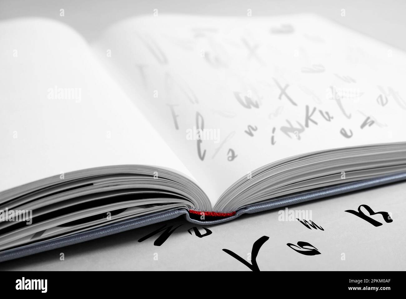 Open book with letters on light grey table, closeup. Dyslexia concept ...