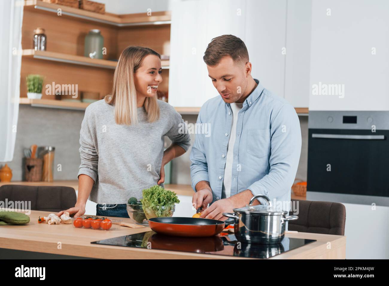 Talking with each other. Couple preparing food at home on the modern ...