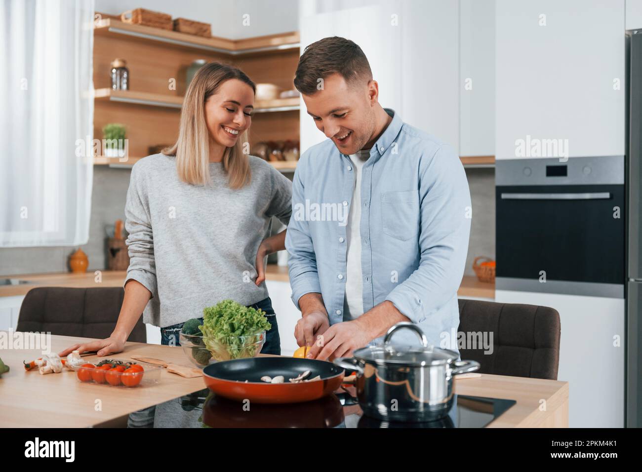 Talking with each other. Couple preparing food at home on the modern ...