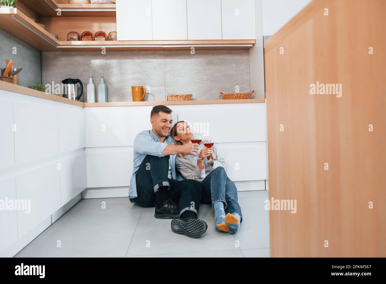Drinking wine. Couple sitting on the floor of modern kitchen Stock ...