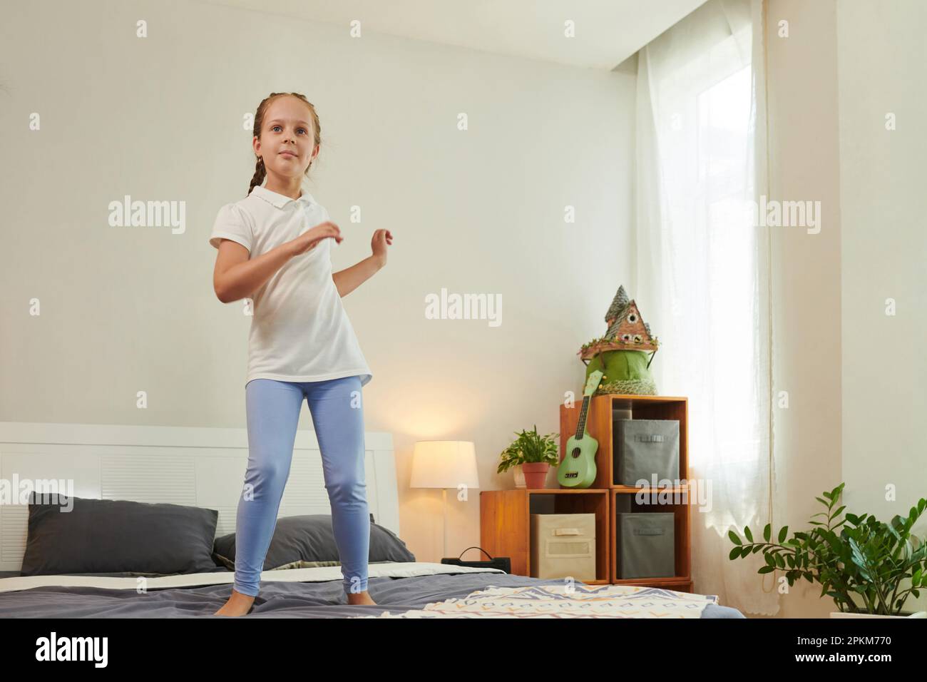 Smiling preteen girl jumping and dancing on bed alone Stock Photo - Alamy