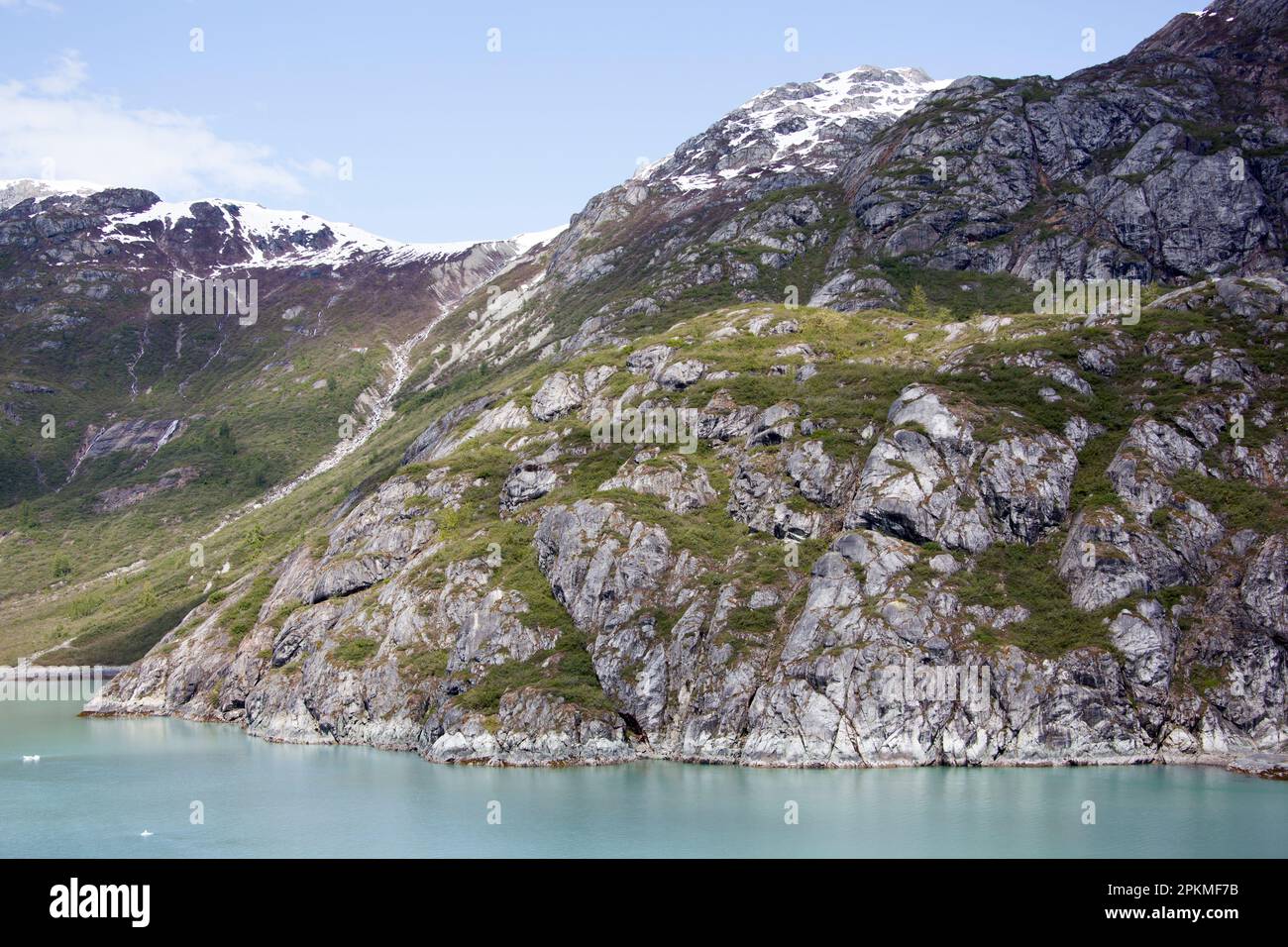 The scenic view of a steep rocky shore and snowy mountains in Summer in ...