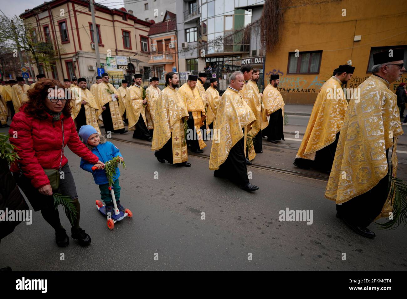 A woman assists a child riding a scooter as Romanian Orthodox priests ...