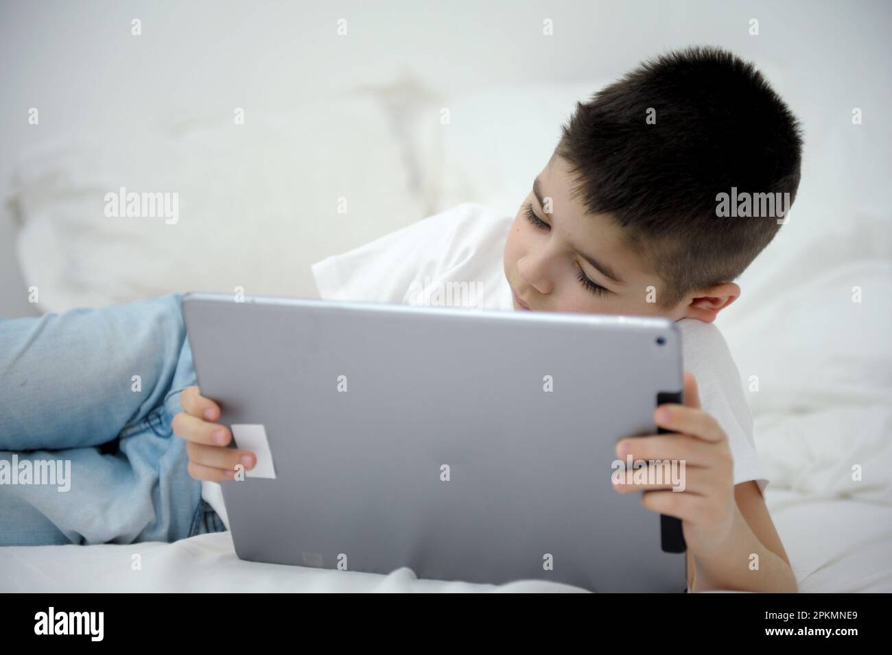 Adorable blond toddler boy laying on the sofa and playing with tablet ...