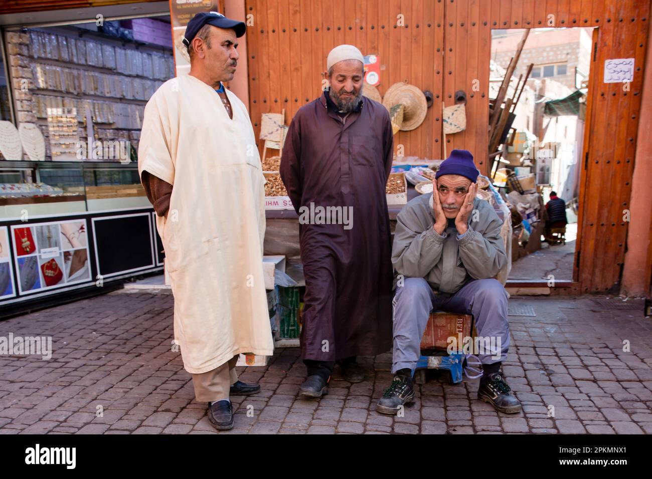 Three men in traditional Moroccan clothing gather outside shops in the ...