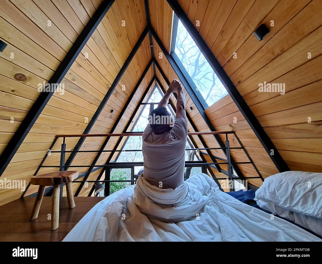 Dark-haired Latino adult man wakes up in the morning on a bed stretches ...