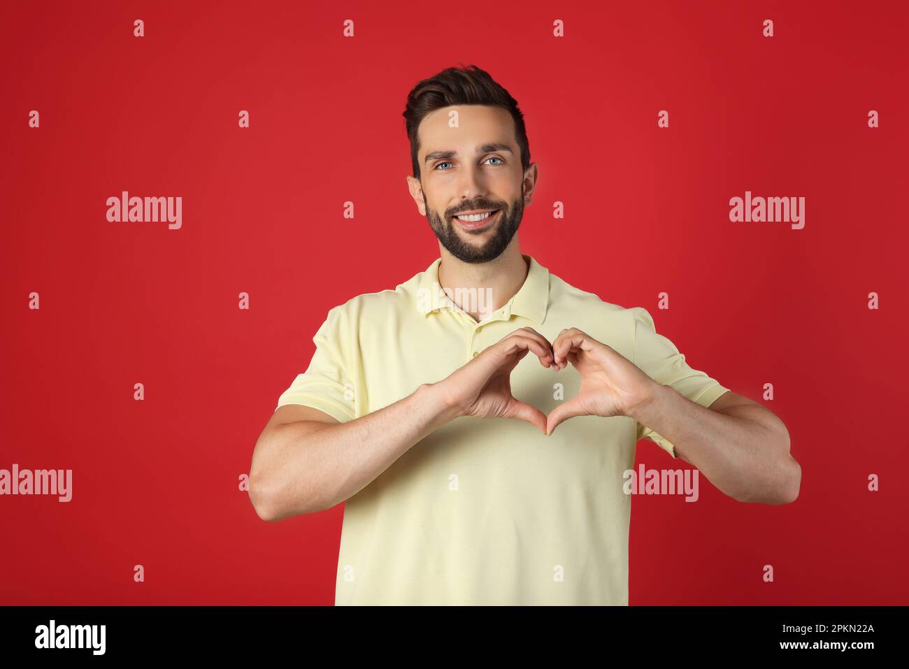 Happy man making heart with hands on red background Stock Photo - Alamy