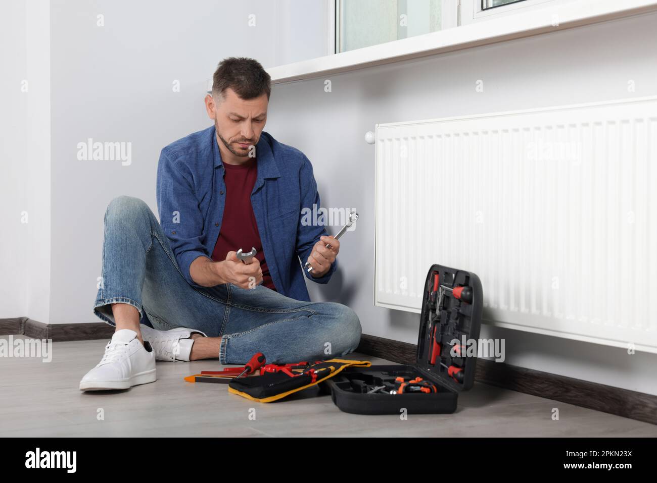 Man choosing wrench near box with tools indoors Stock Photo - Alamy