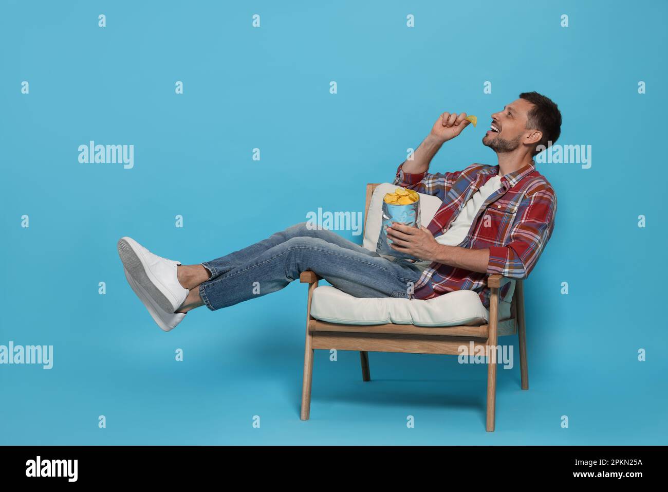 Handsome man eating potato chips on light blue background Stock Photo ...