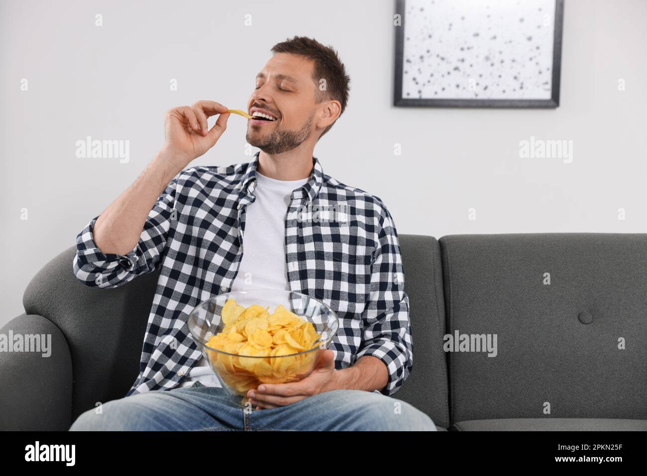 Handsome man eating potato chips on sofa at home Stock Photo - Alamy