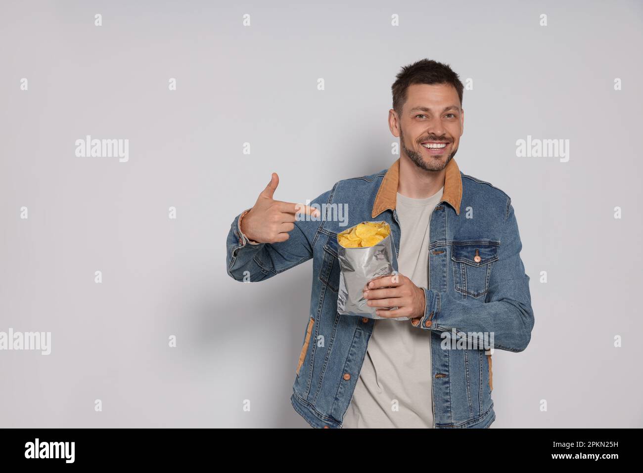 Handsome man pointing on potato chips against light grey background ...