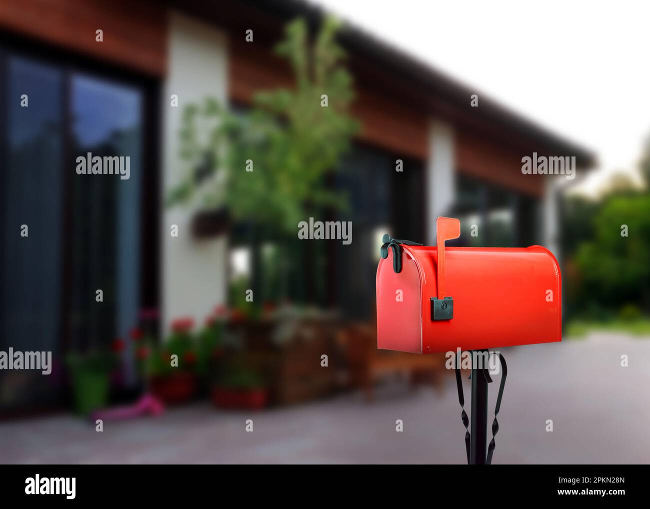Red letter box and blurred view of modern house on sunny day, space for ...