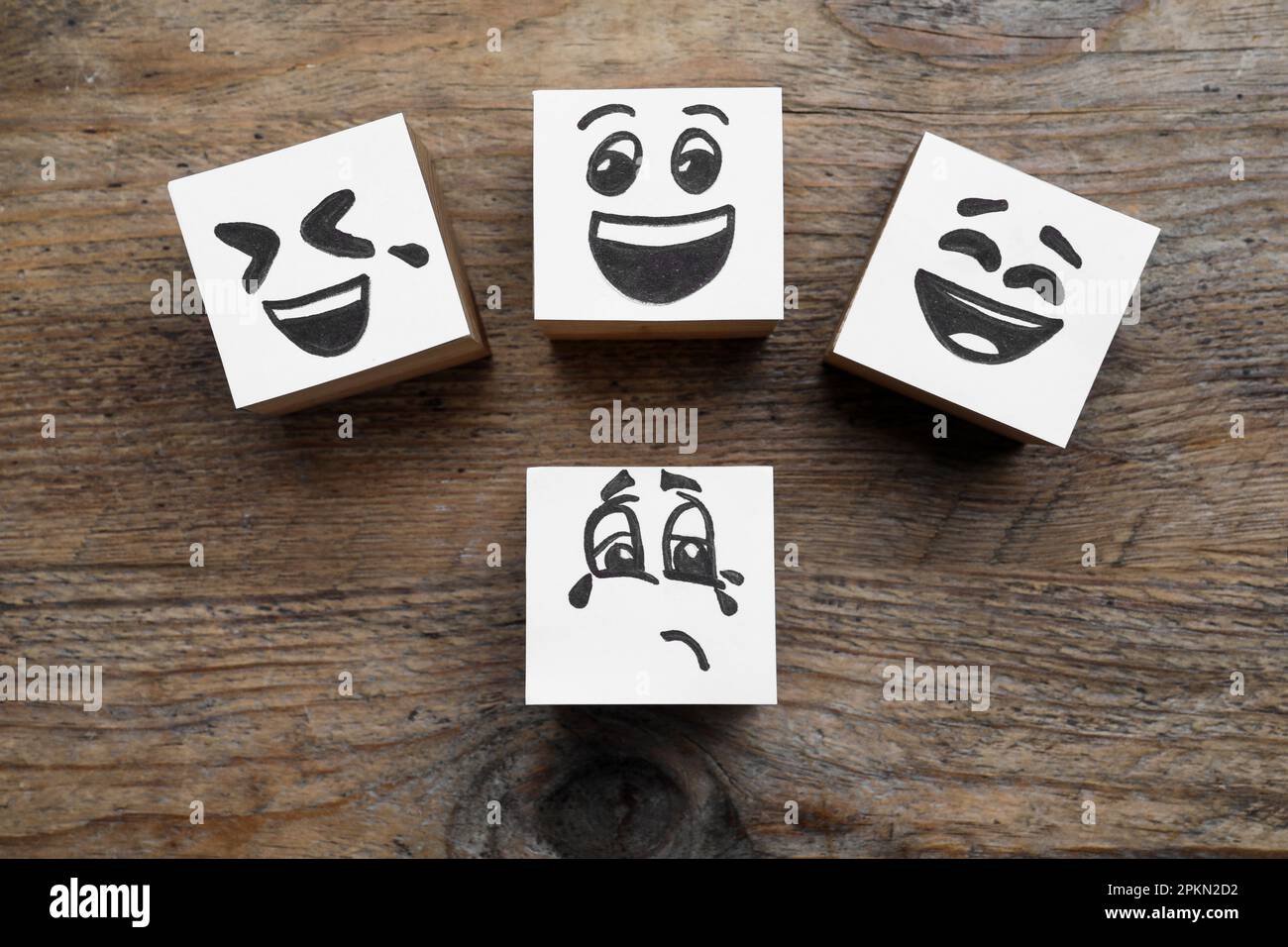 Cubes with sad and funny faces on wooden table, flat lay. Bullying ...