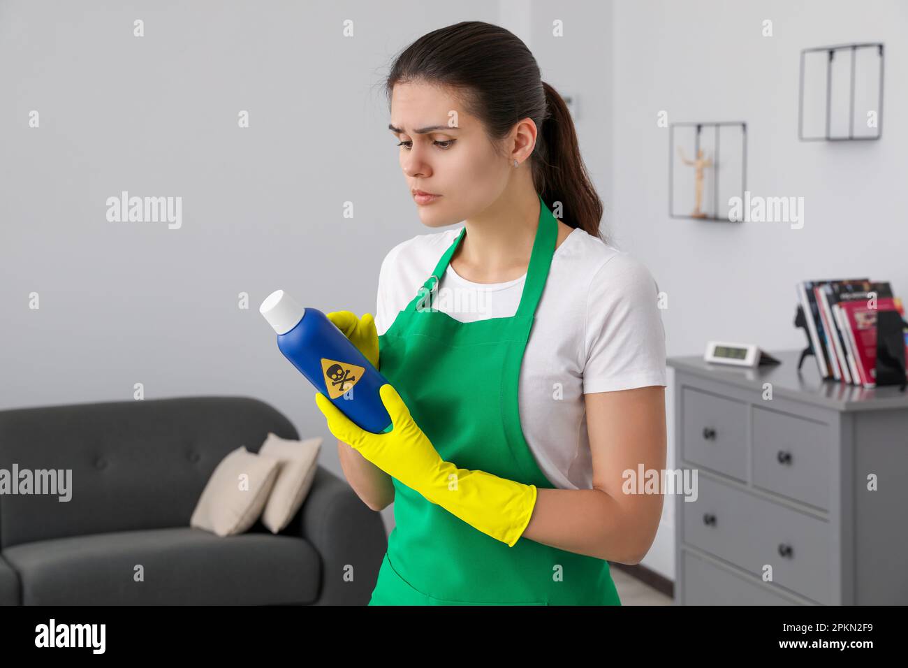 Woman looking at bottle of toxic household chemical with warning sign ...