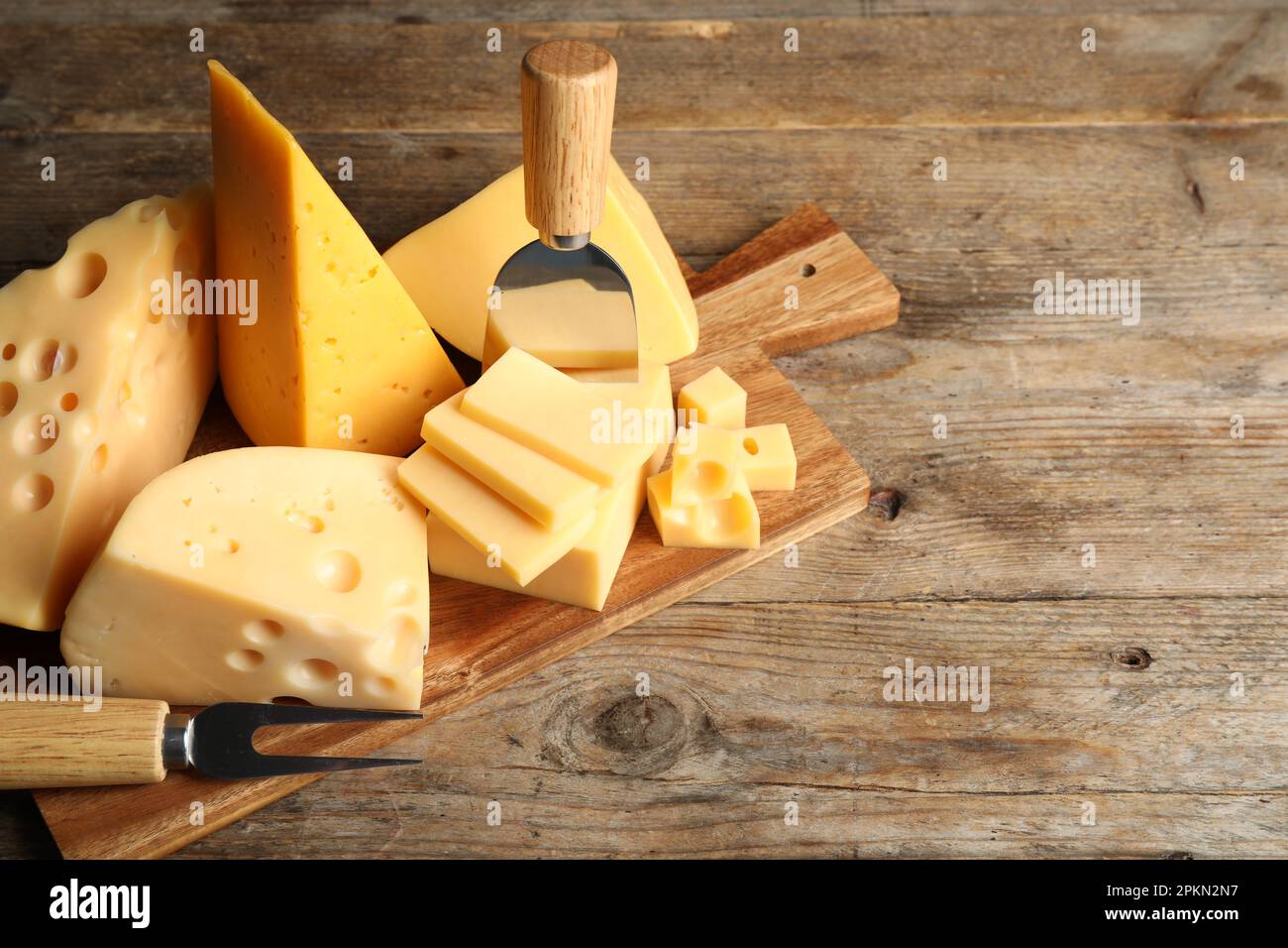 Different sorts of cheese, fork and knife on wooden table. Space for ...