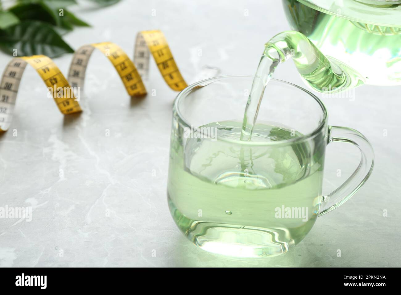 Pouring herbal diet tea into cup at light table with measuring tape ...