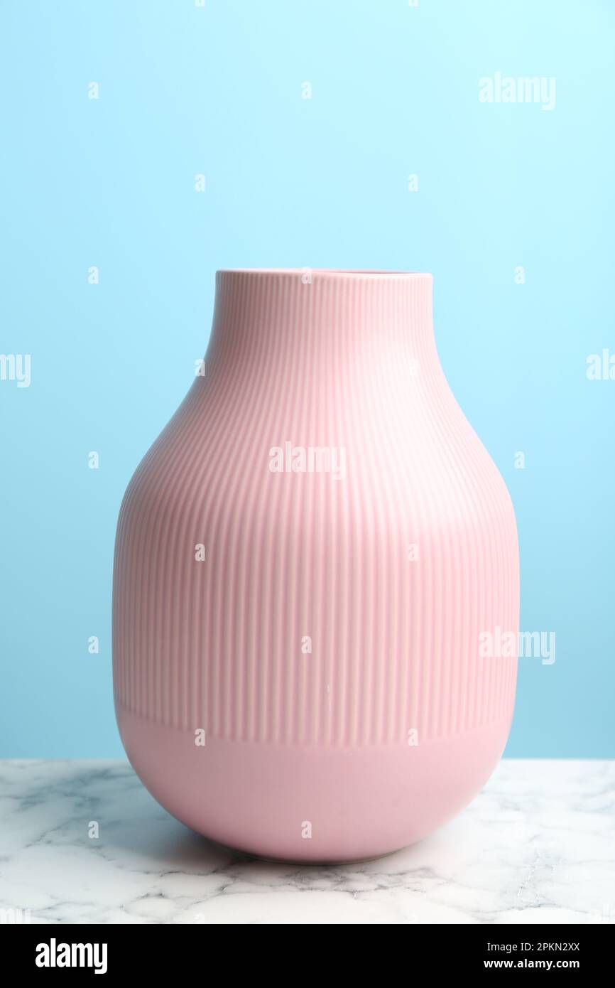 Stylish pink ceramic vase on white marble table against light blue ...