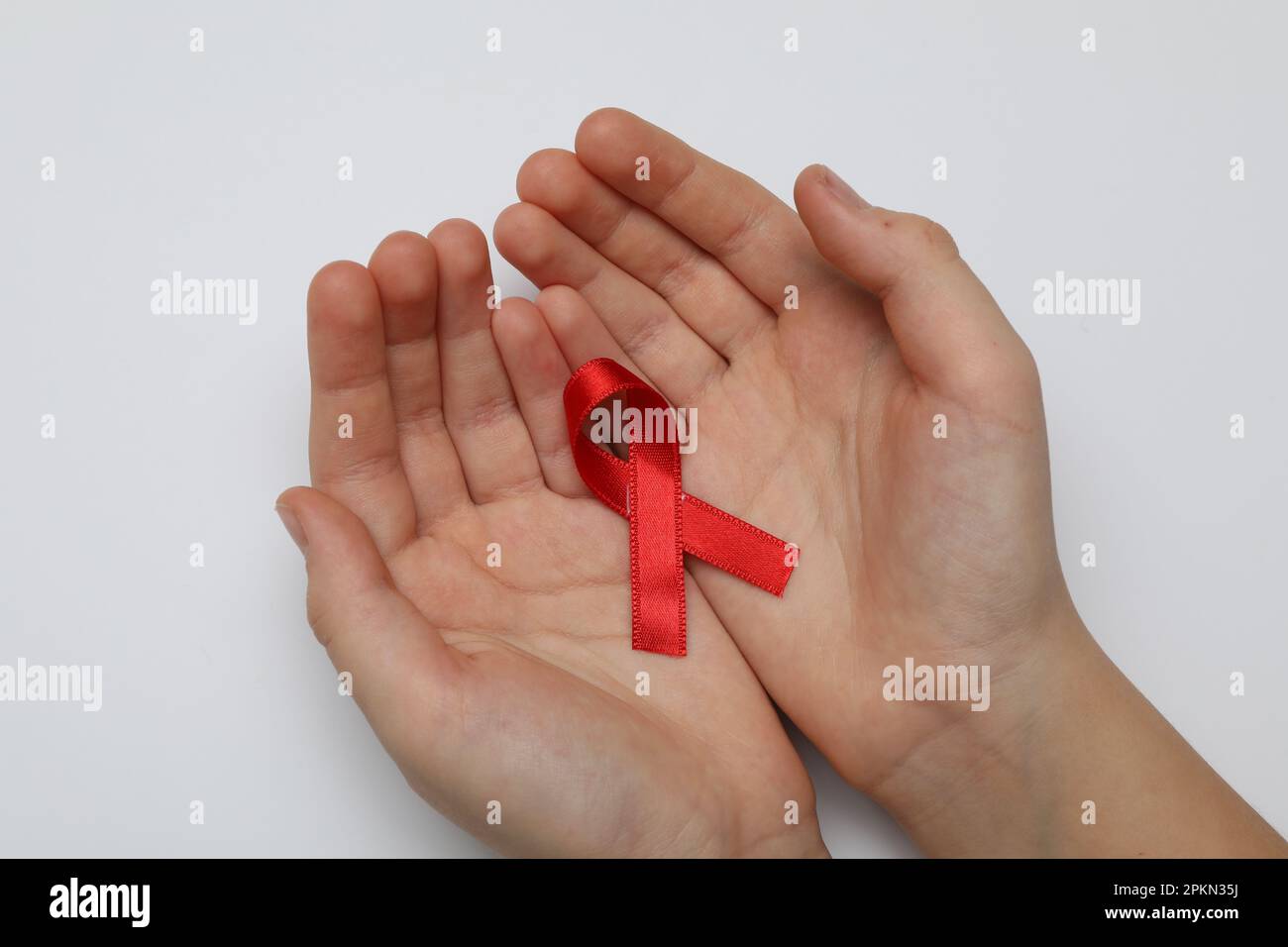 Little girl holding red ribbon on white background, closeup. AIDS ...