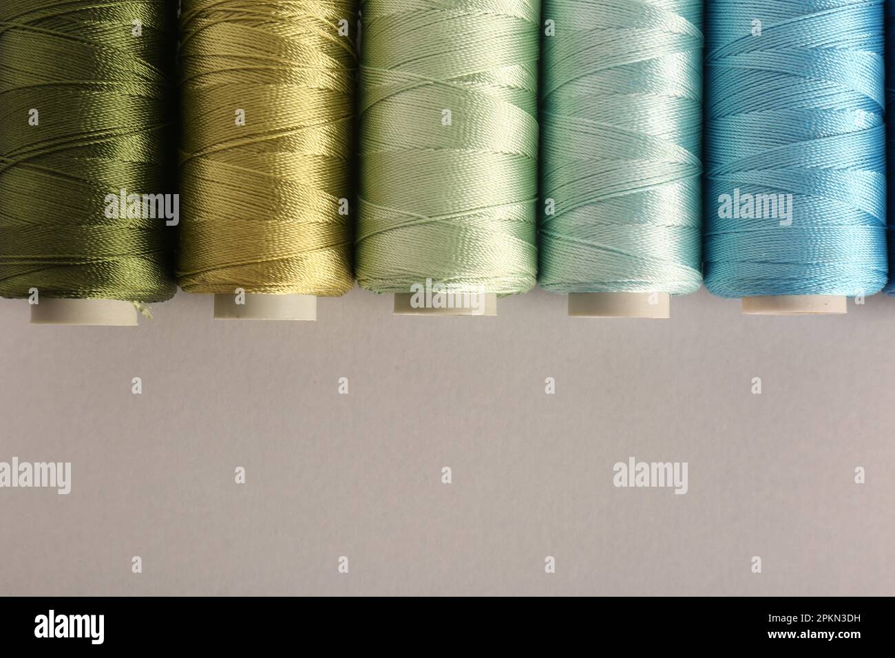 Different colorful sewing threads on light grey background, flat lay ...