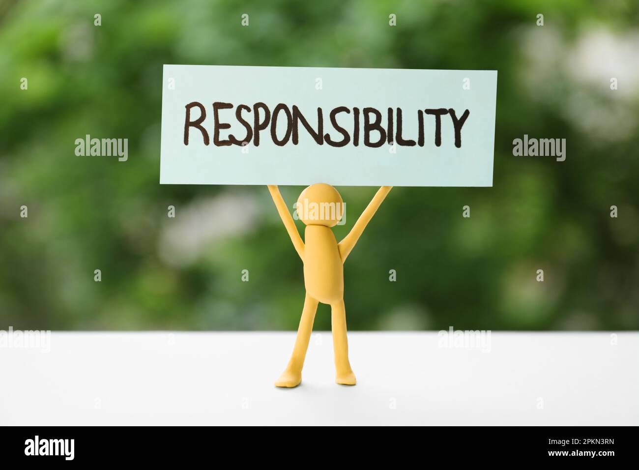 Plasticine human figure holding card with word Responsibility on white ...