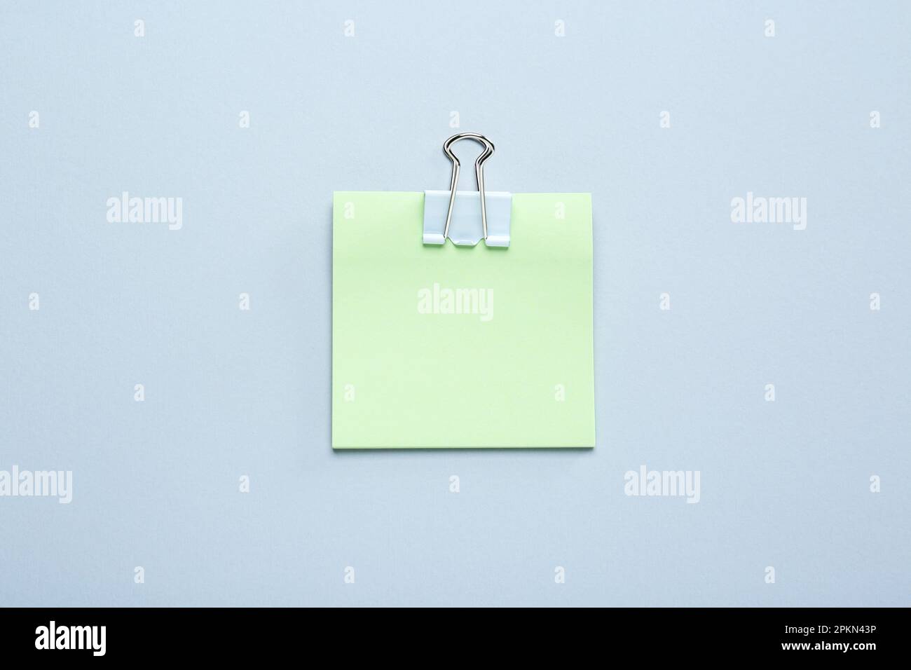 Blank light green note with white paper clamp on grey background, top ...