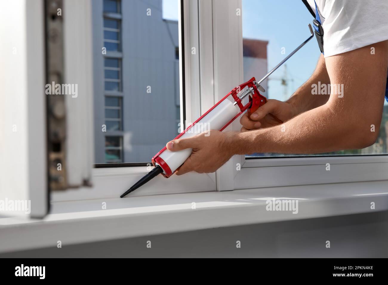 Worker sealing plastic window with caulk indoors, closeup. Installation ...