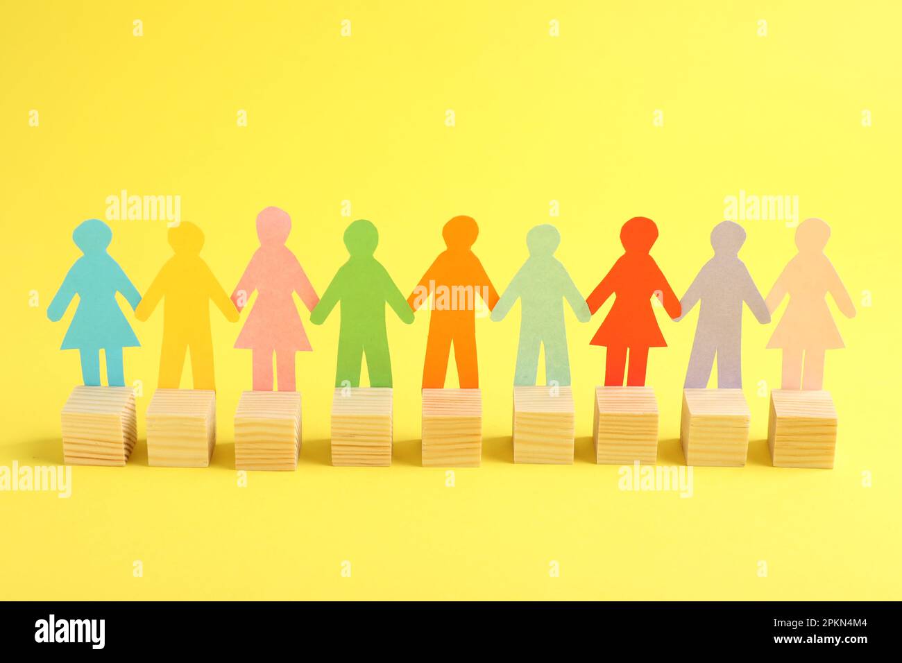 Paper human figures with wooden cubes on yellow background. Diversity ...