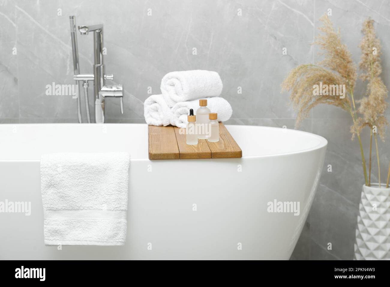 Rolled bath towels and personal care products on tub tray in bathroom ...