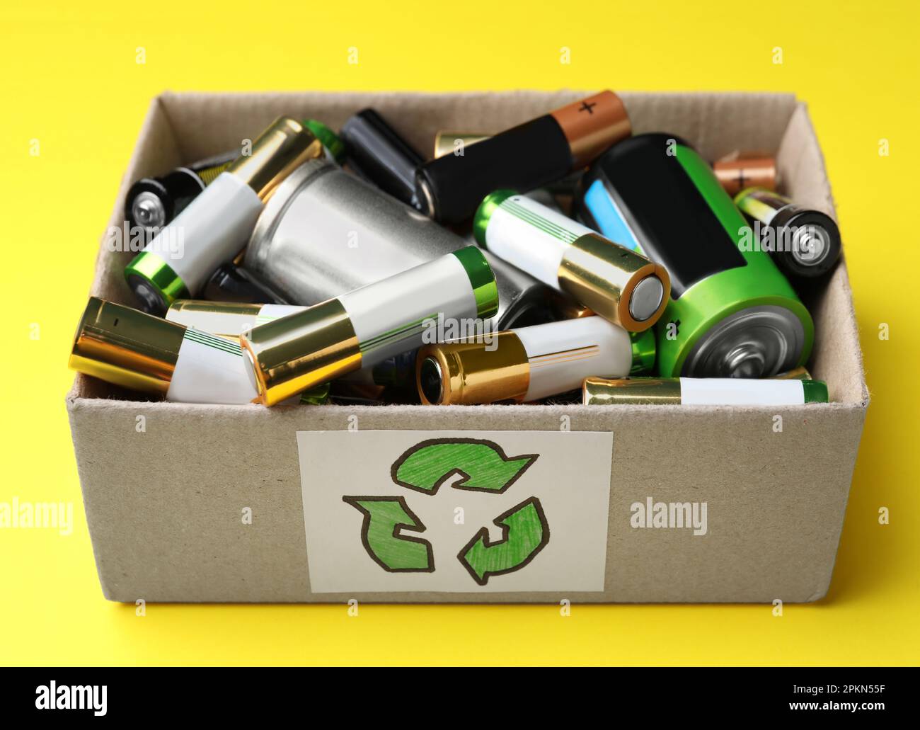 Used batteries in cardboard box with recycling symbol on yellow ...
